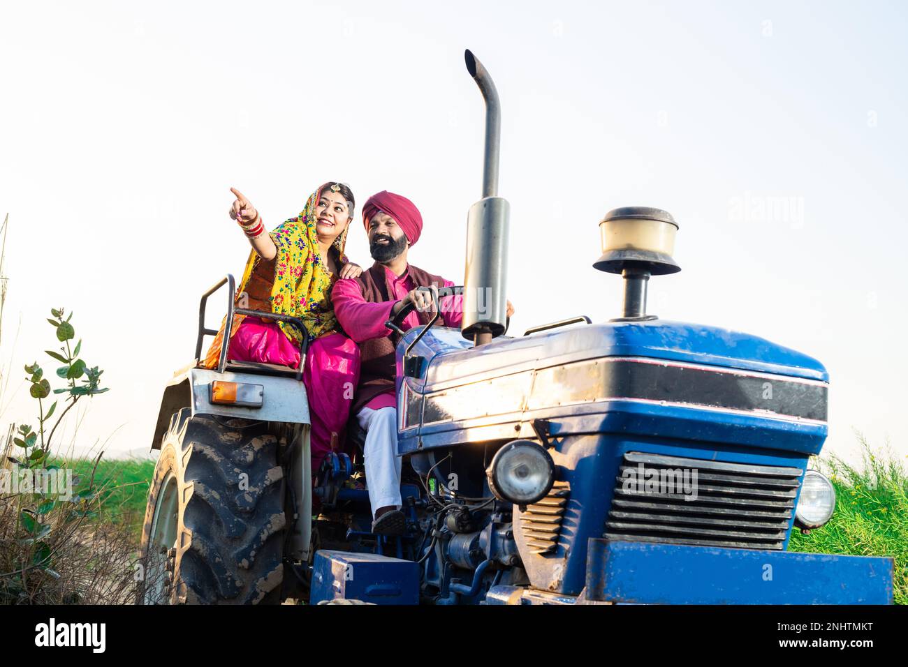 Happy punjab sikh farmer couple driving tractor pointing at agriculture ...