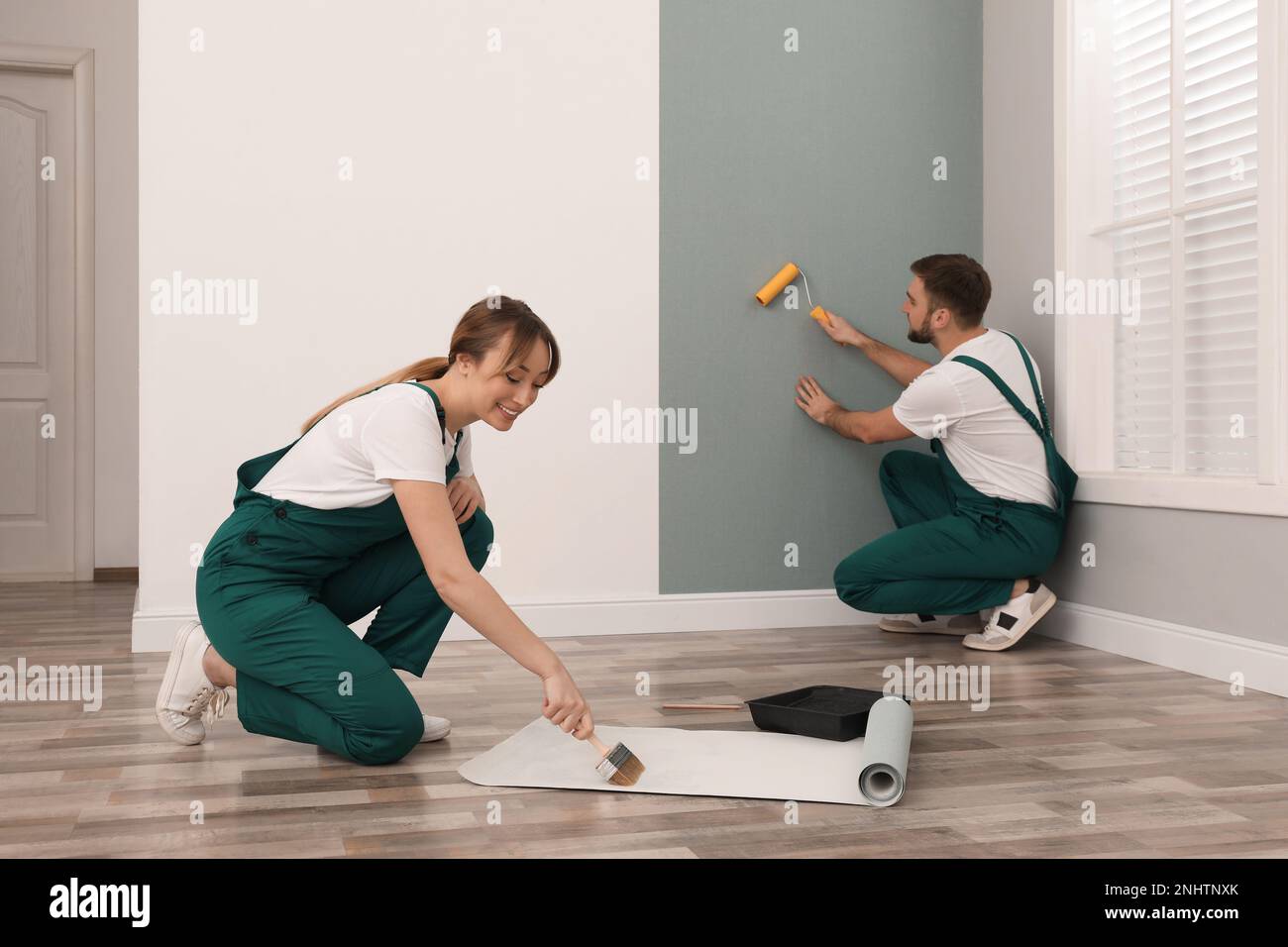 Woman applying glue onto wall paper while man hanging sheet indoors ...