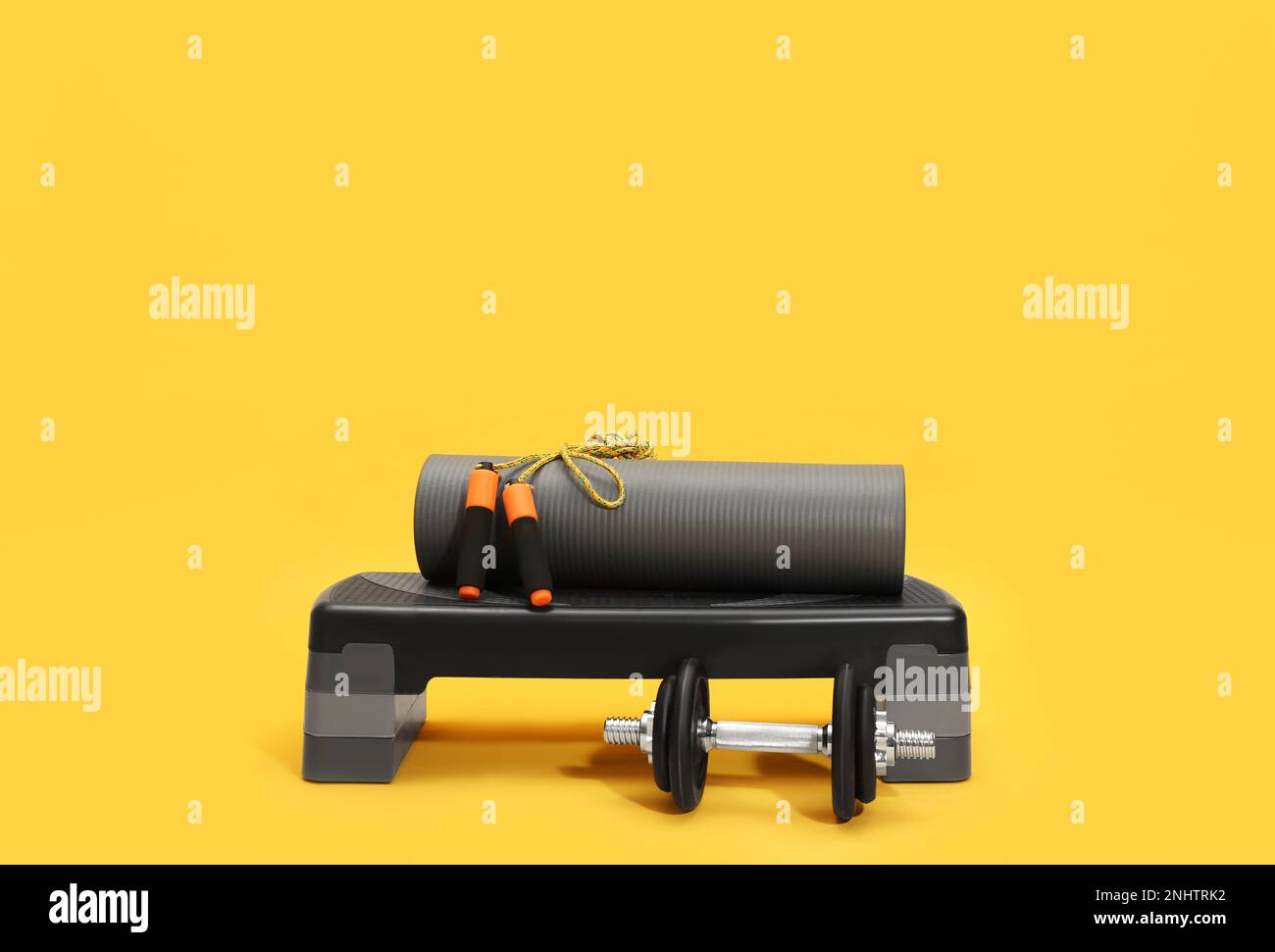 Step platform, dumbbell, mat and jump rope on yellow background. Sports ...