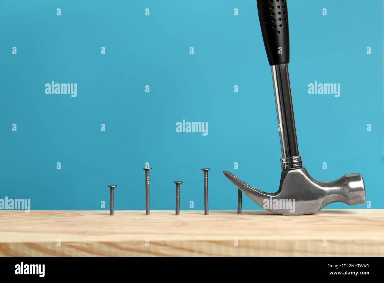 Hammer pulling metal nail out of wooden surface against light blue ...