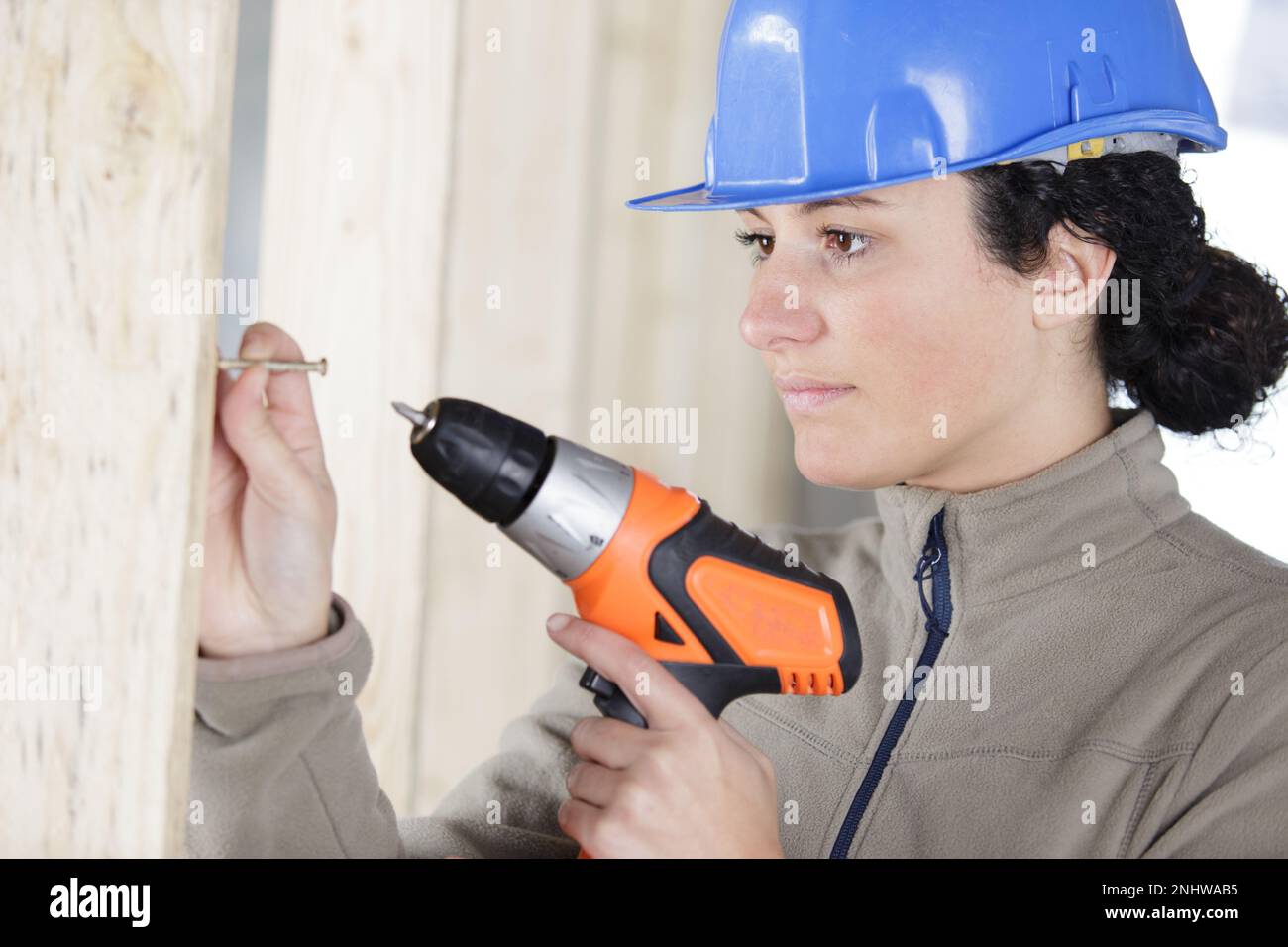 female builder using cordless screwdiver to insert screw in wall Stock ...