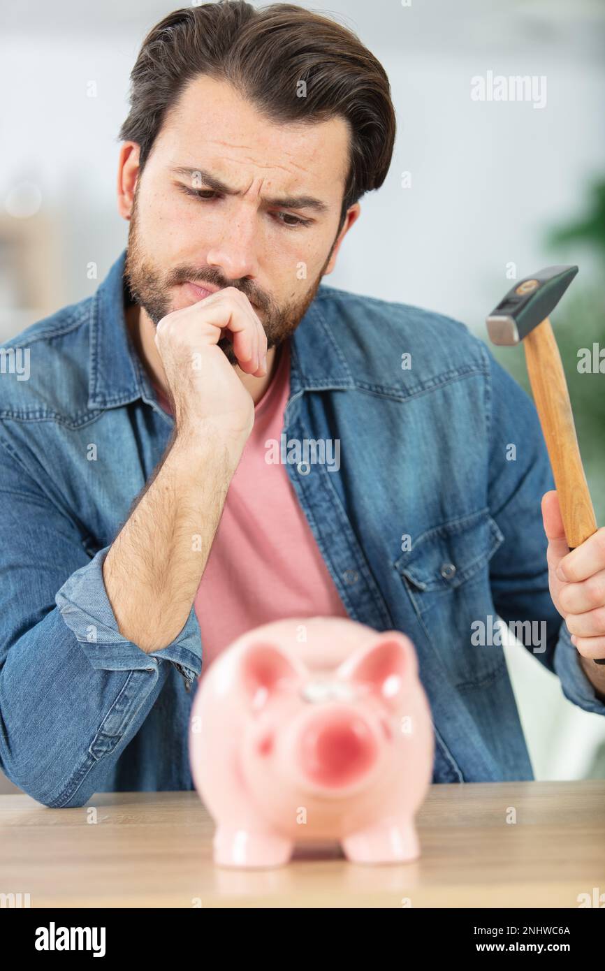 helpless man with piggy bank and hammer Stock Photo - Alamy