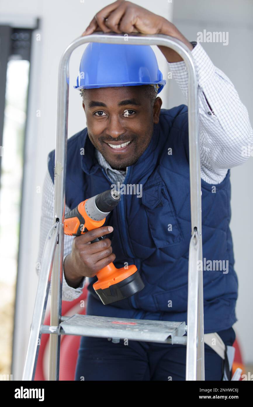 happy male builder standing on ladder with drill Stock Photo - Alamy