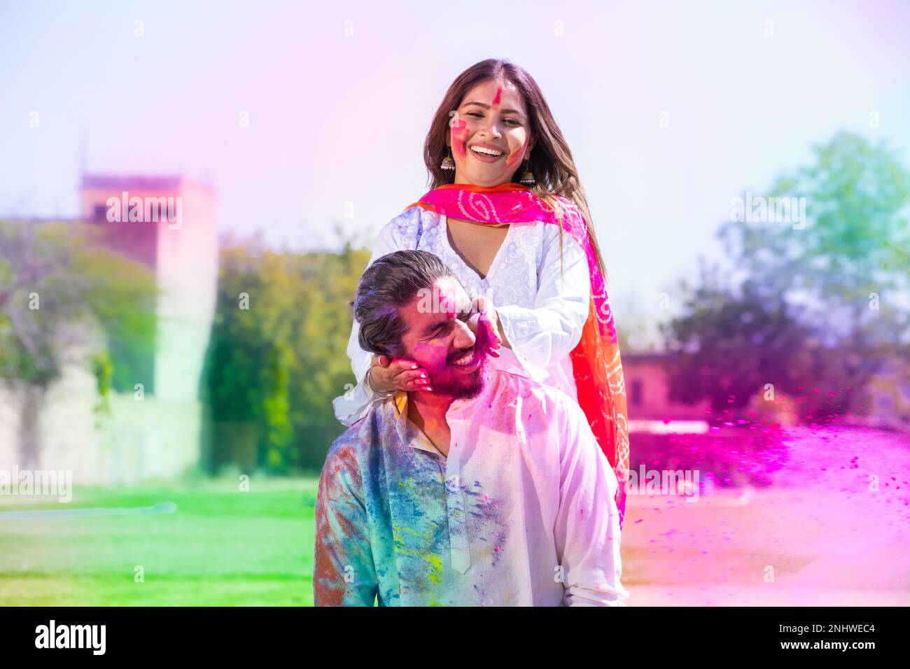 Cheerful young Indian couple playing with colorful powder color or ...