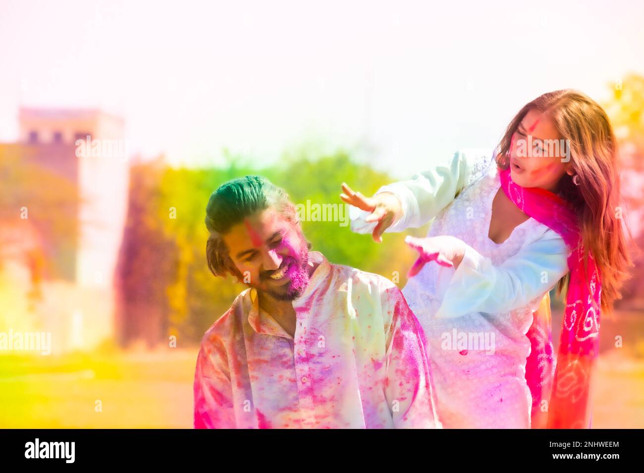 Cheerful young Indian couple playing with colorful powder color or ...