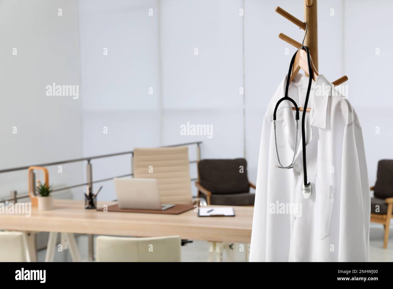 Modern doctor's workplace with wooden table and white coat hanging on ...