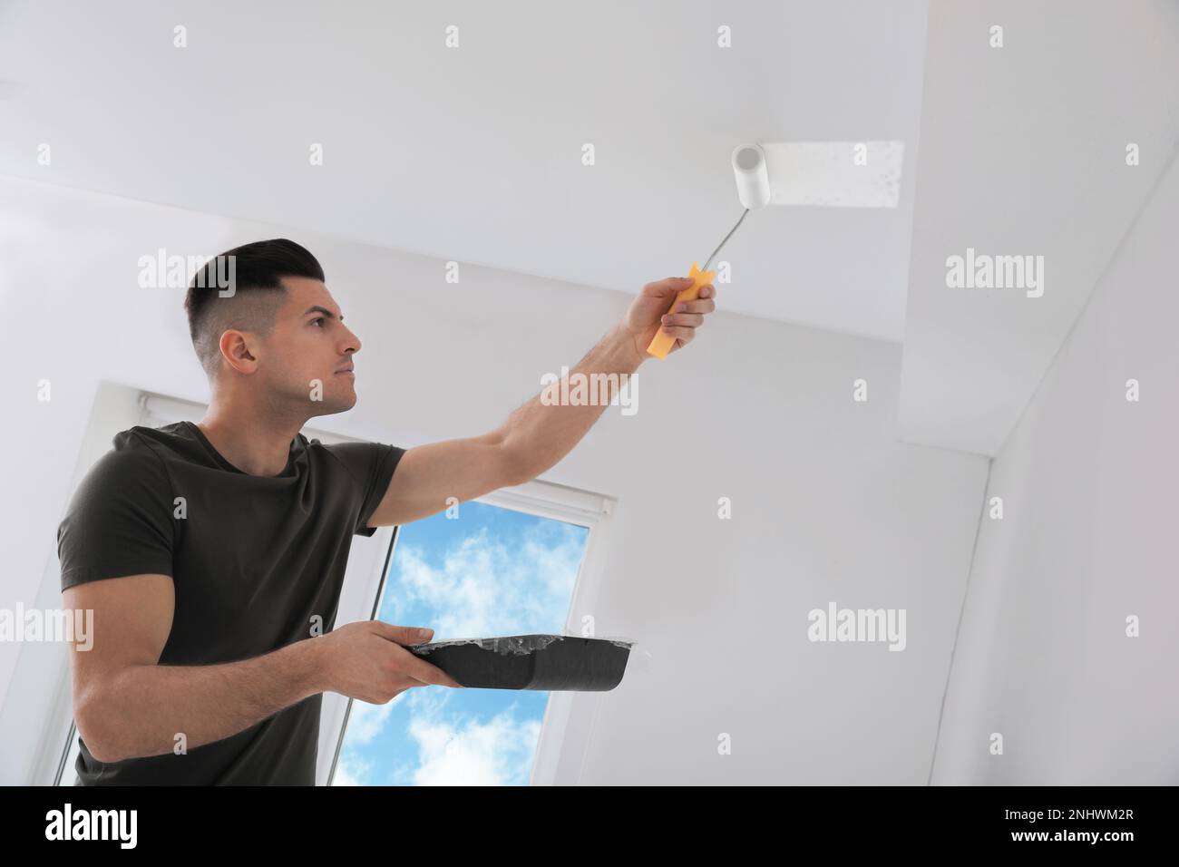 Man painting ceiling with roller in room Stock Photo - Alamy