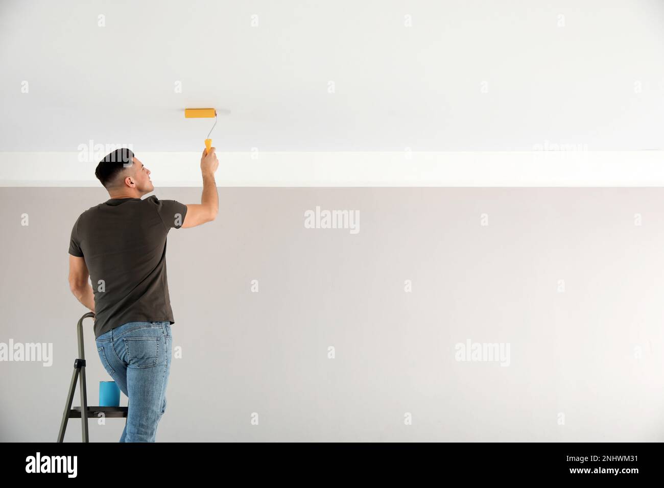 Man painting ceiling with roller in room, back view. Space for text ...
