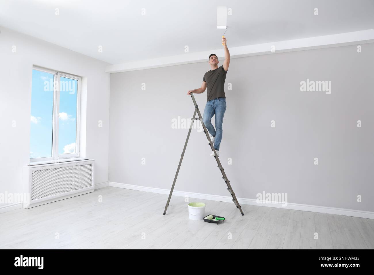 Man painting ceiling with roller on step ladder in room Stock Photo - Alamy