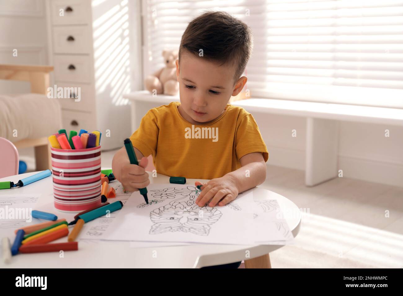 Cute child coloring drawing at table in room Stock Photo - Alamy