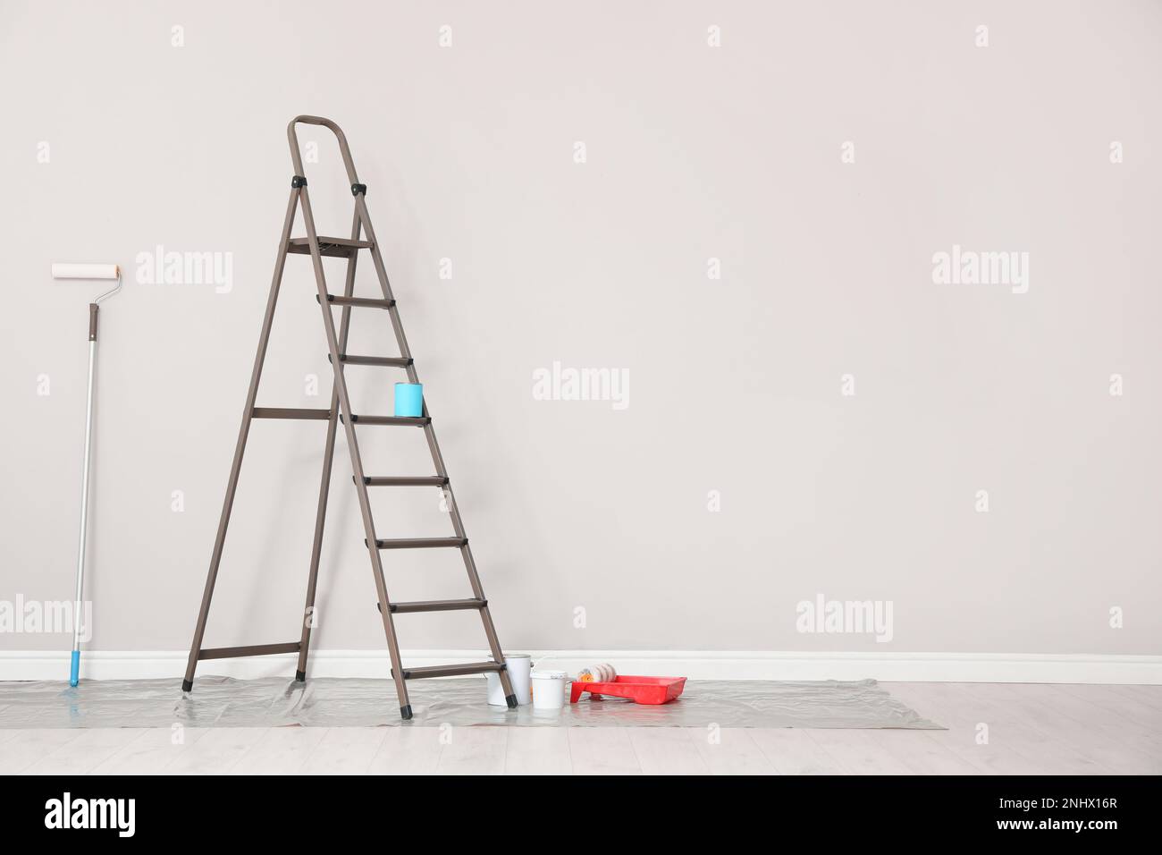 Decorator's tools and ladder near white wall indoors, space for text ...