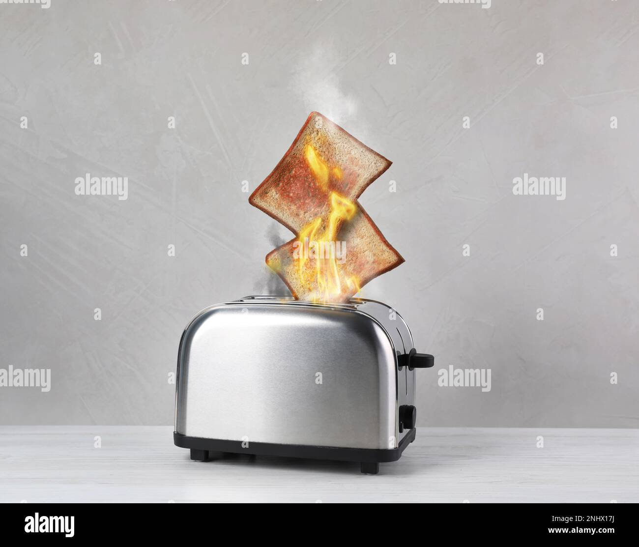 Toaster flaming up while cooking slices of bread on white wooden table ...