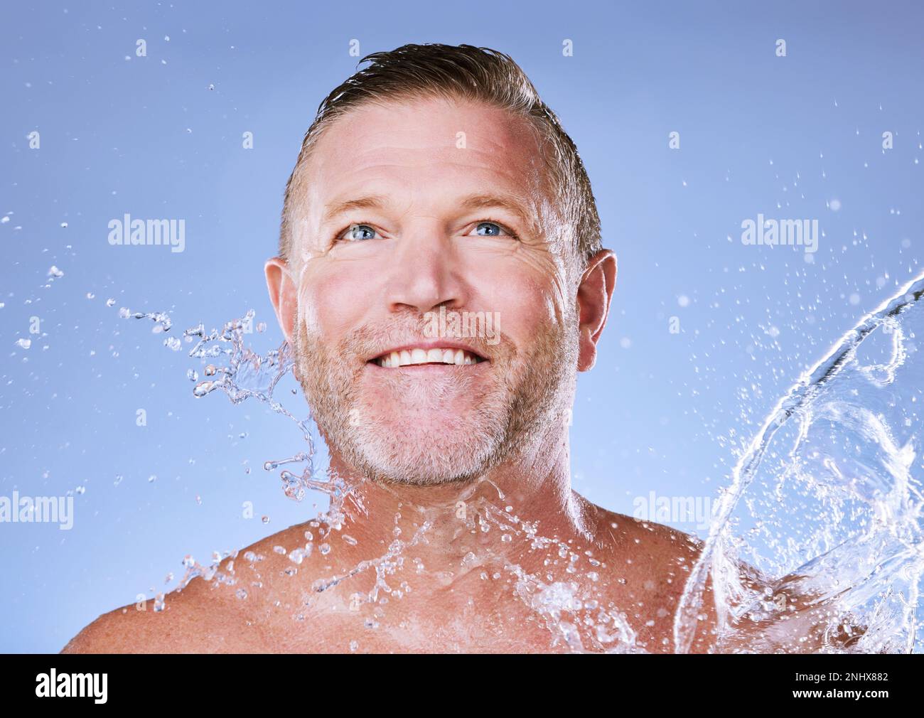 Wellness, water splash and senior man cleaning, morning routine and washing on blue studio ...