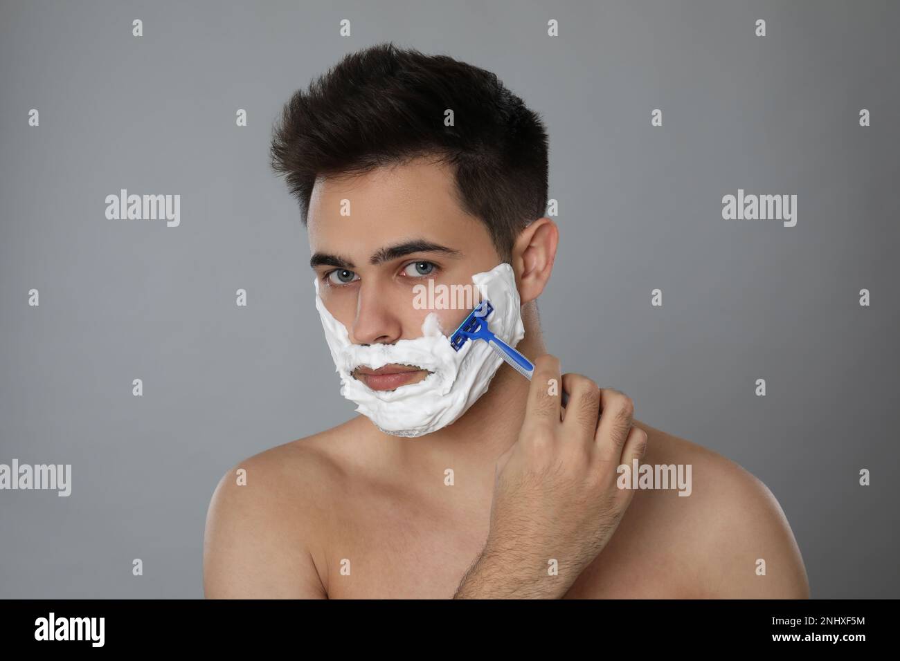 Handsome young man shaving with razor on grey background Stock Photo ...
