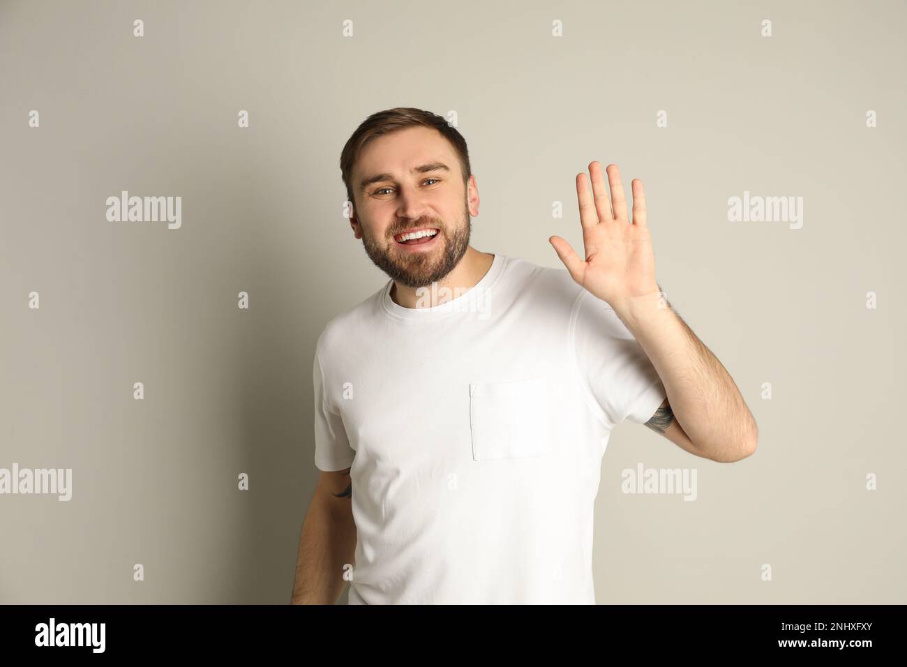 Happy young man waving to say hello on light grey background Stock ...