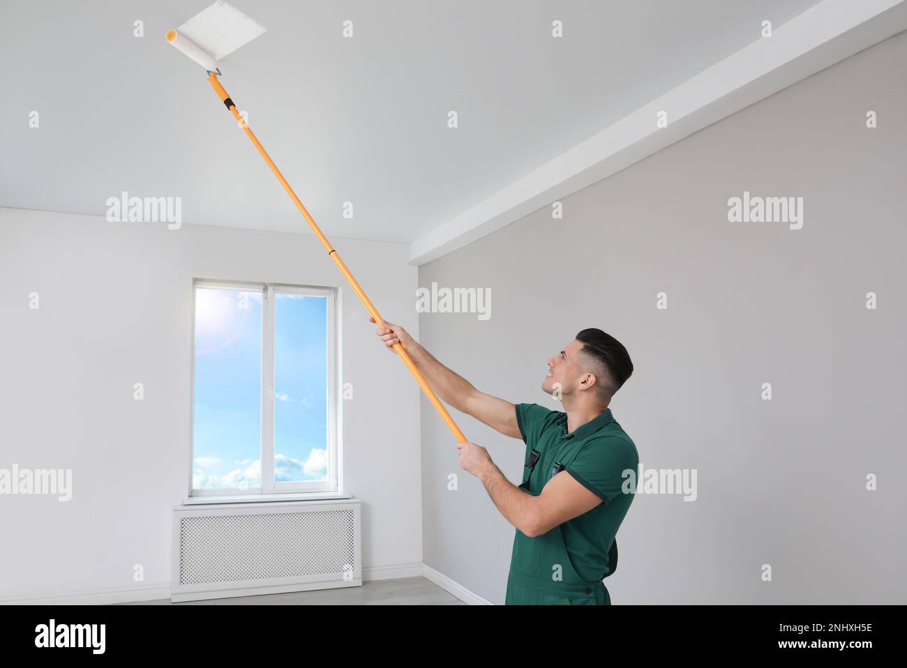 Man painting ceiling with roller in room Stock Photo - Alamy