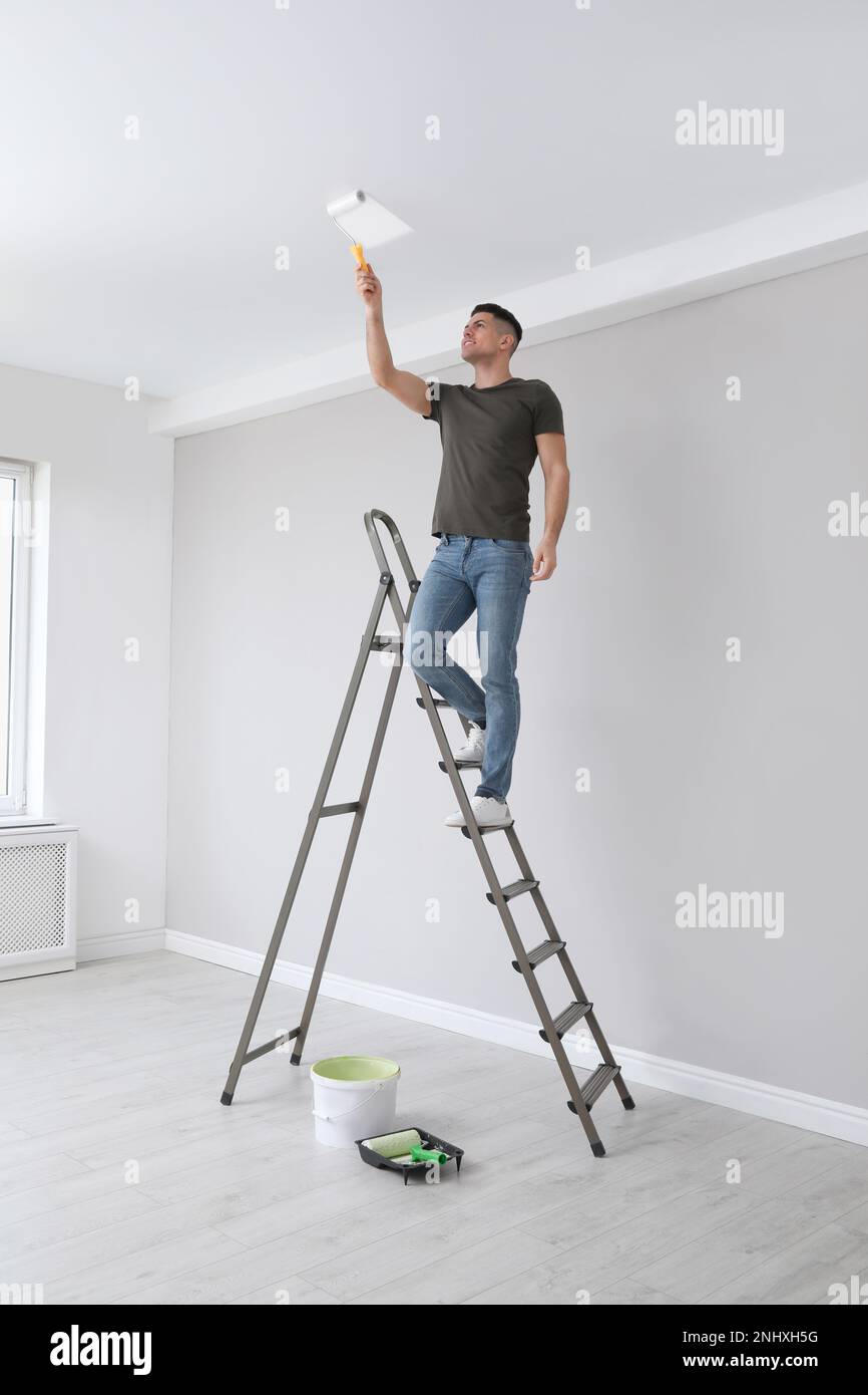 Man painting ceiling with roller on step ladder in room Stock Photo - Alamy