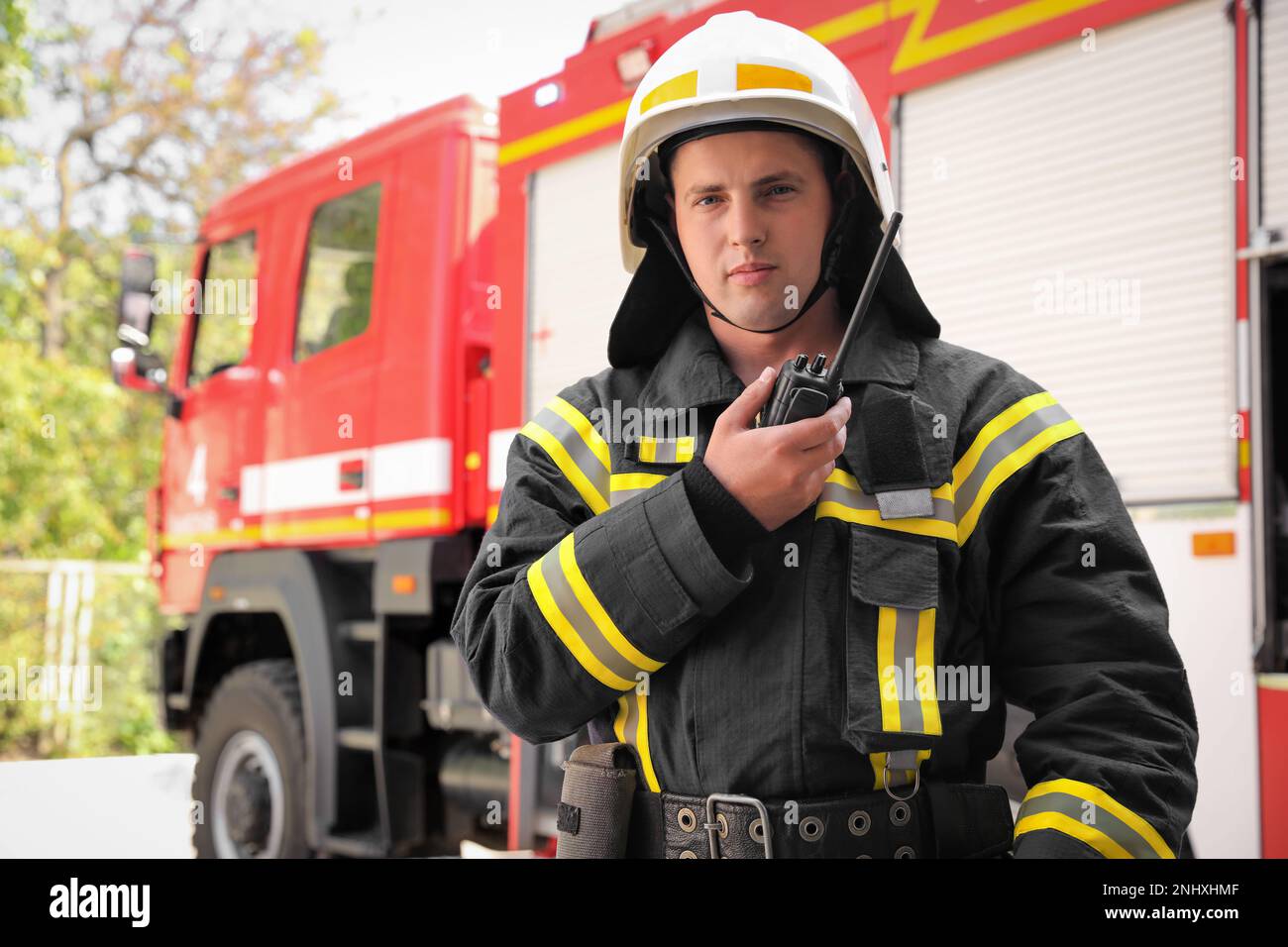 Portrait of firefighter in uniform with portable radio set near fire ...