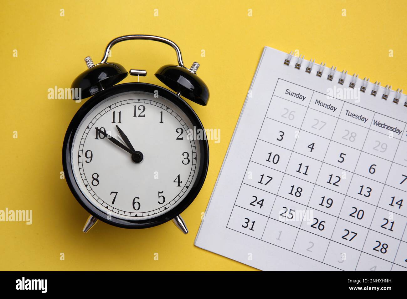 Alarm clock and calendar on yellow background, flat lay. Reminder ...