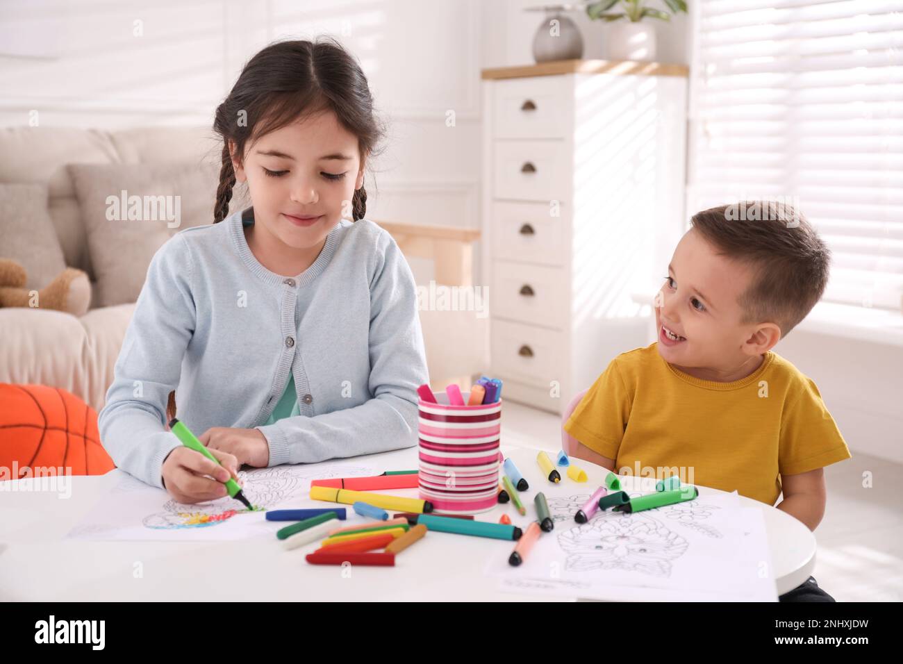 Cute children coloring drawings at table in room Stock Photo - Alamy