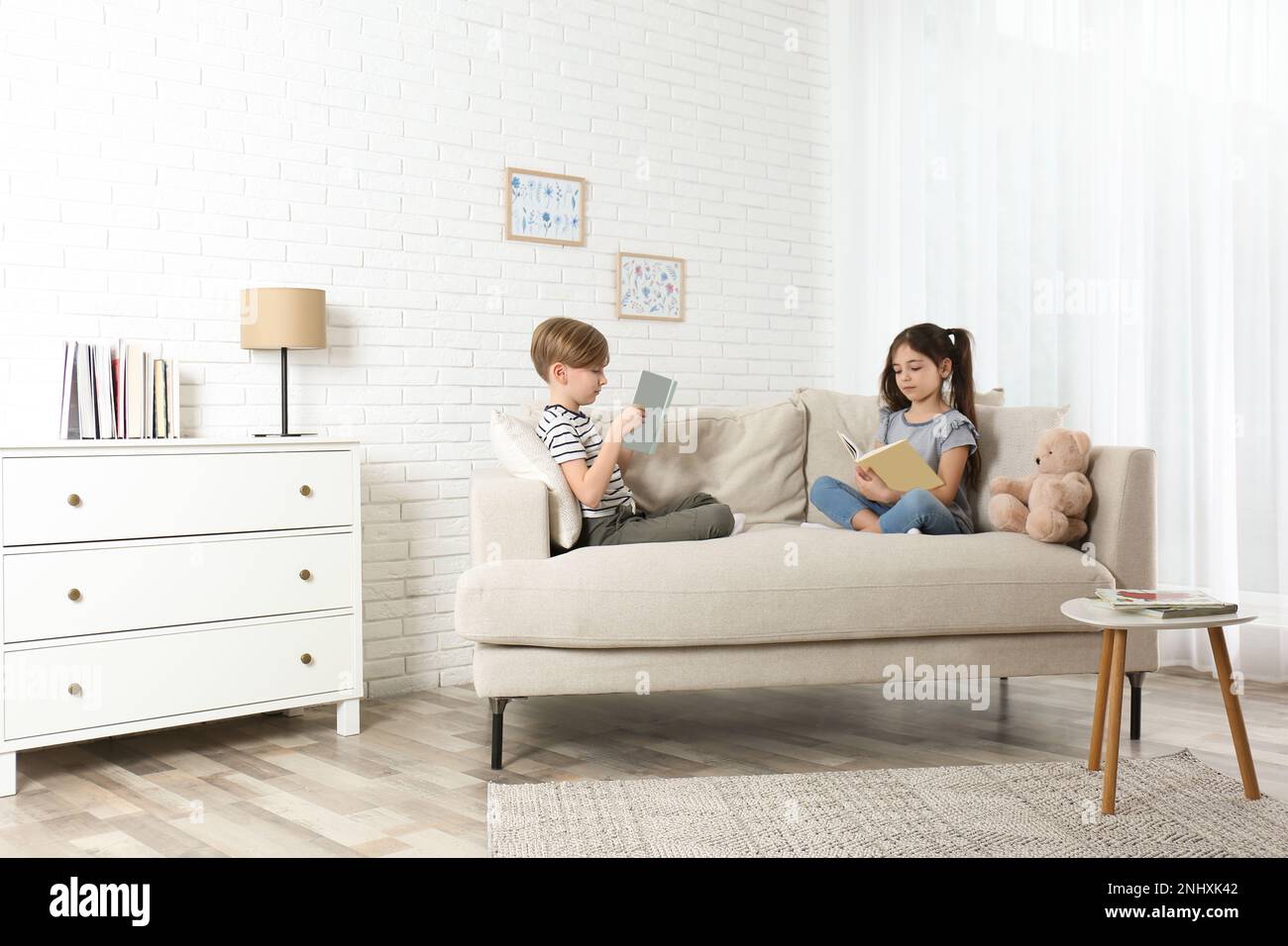 Little boy and girl reading books on sofa at home Stock Photo - Alamy