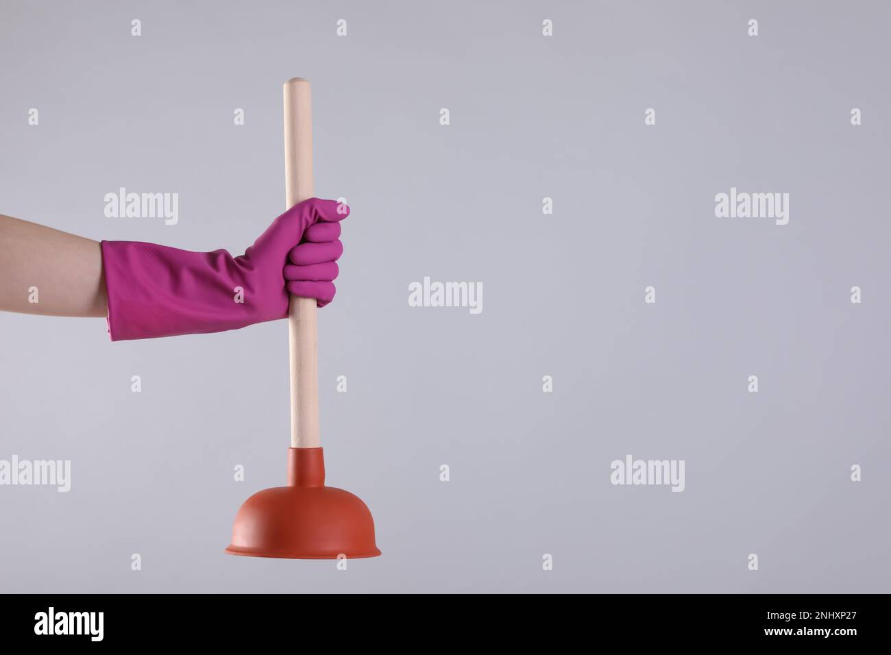 Woman holding plunger on light grey background, closeup. Space for text ...