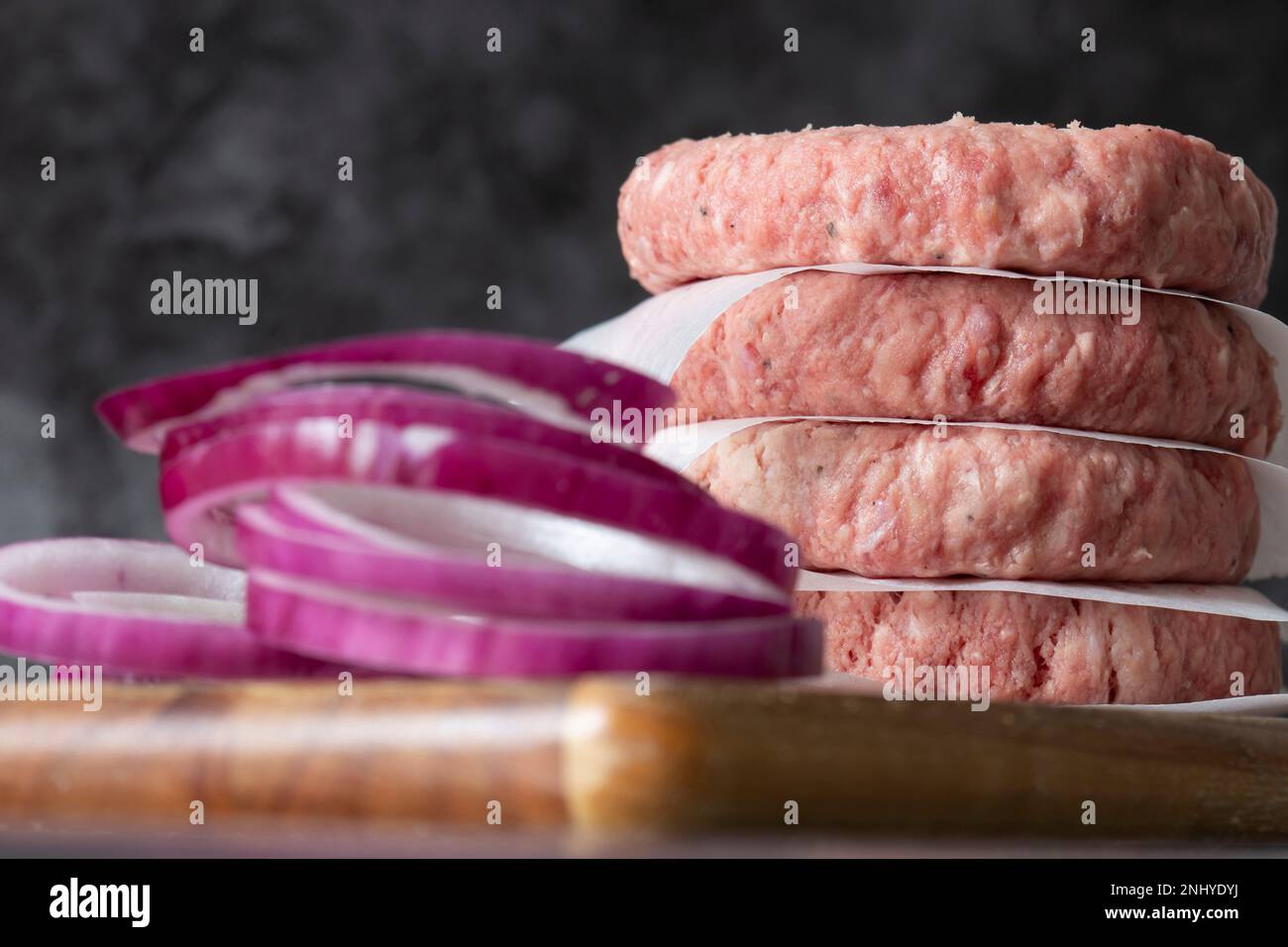 Raw beef burgers stacked on a wood cutting board, separated with ...
