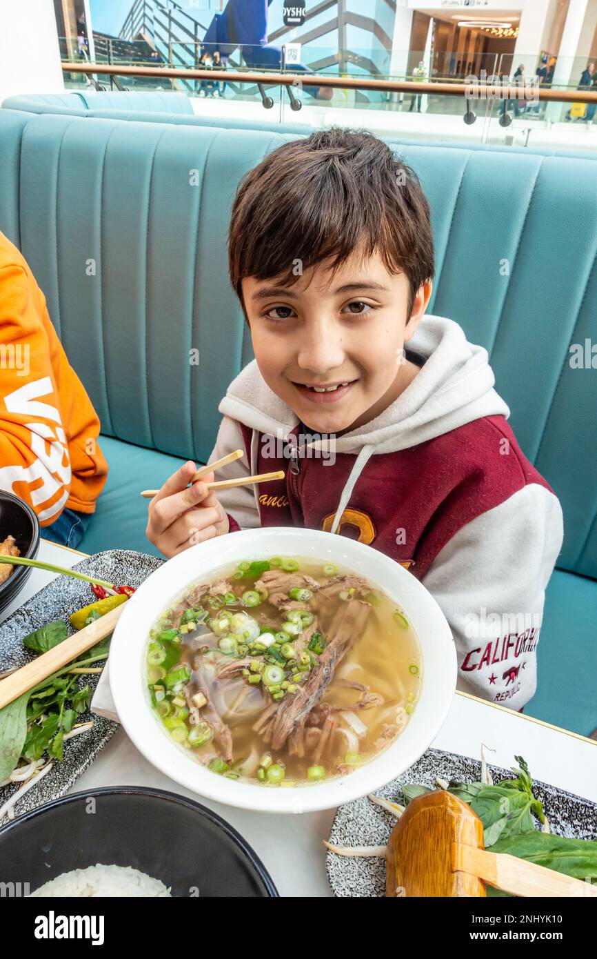 A boy eating a bowl of pho, a Vietnamese soup made with beef brisket ...