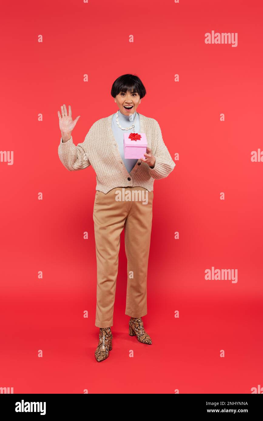 full length of excited asian woman in stylish clothes holding present ...