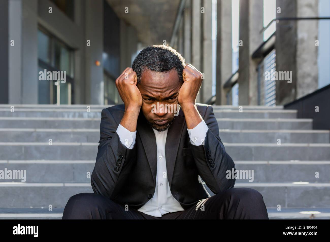 Sad african american businessman sitting on stairs outside office ...