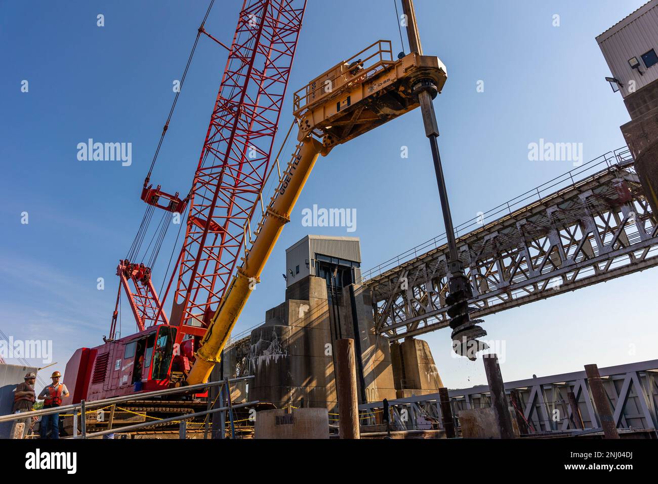 A construction fleet uses a crane-mounted drill do burrow holes into ...