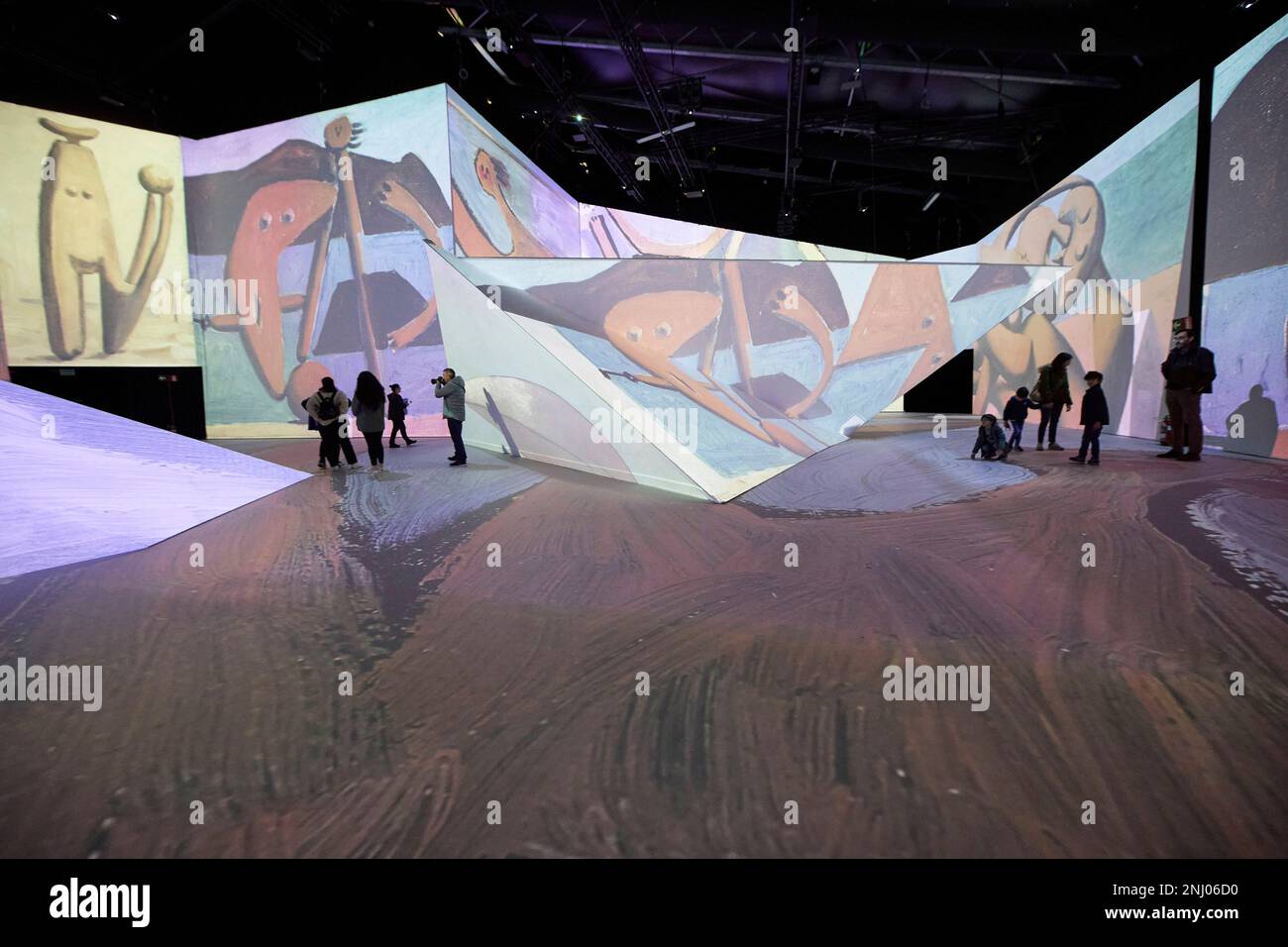 Several people walk through a room where works by Picasso are projected ...