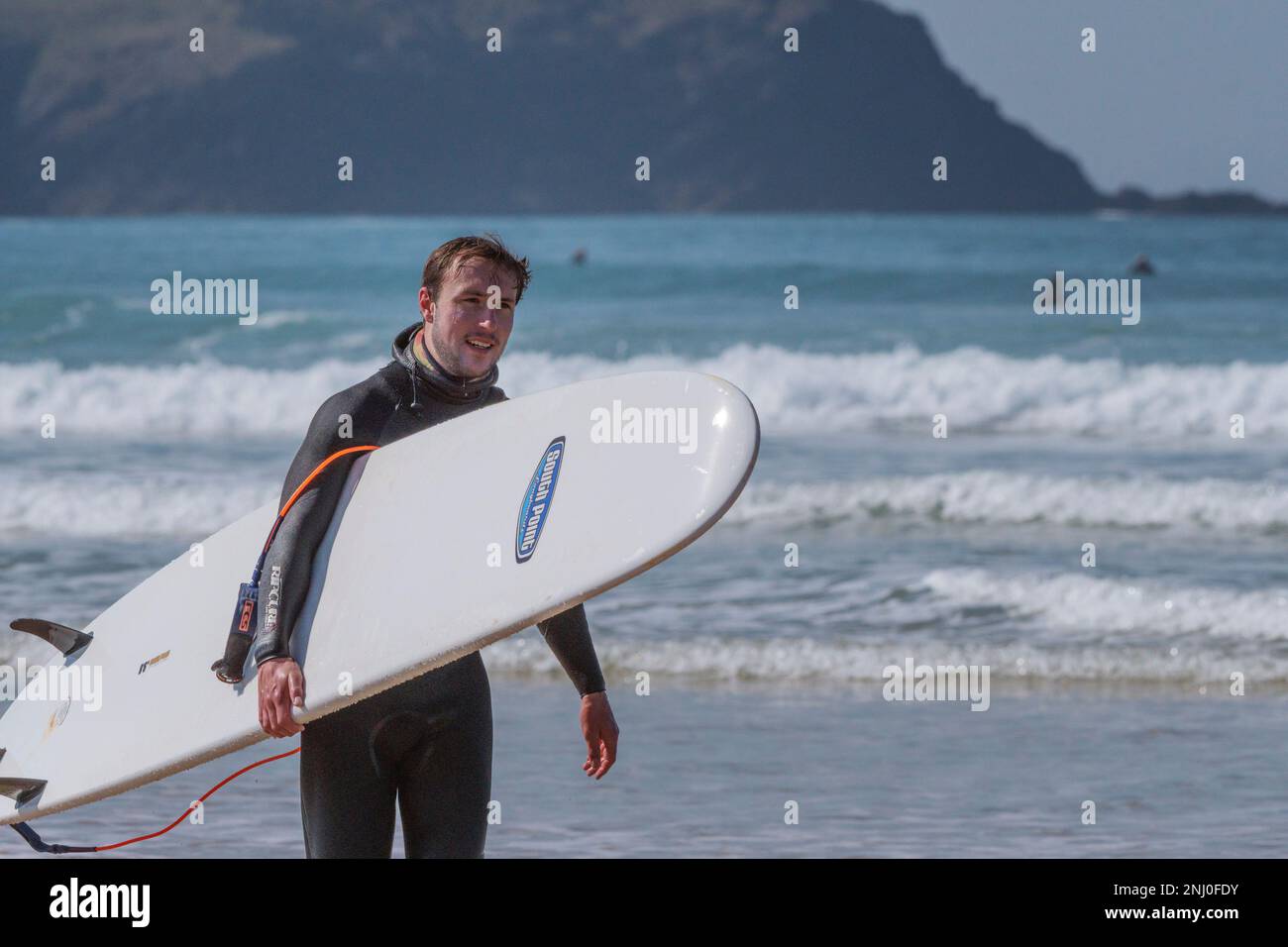 A sufer carrying his surfboard and walking on Fistral Beach in Newquay ...