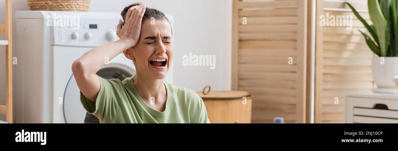 sad woman touching head and crying in laundry room, banner,stock image ...