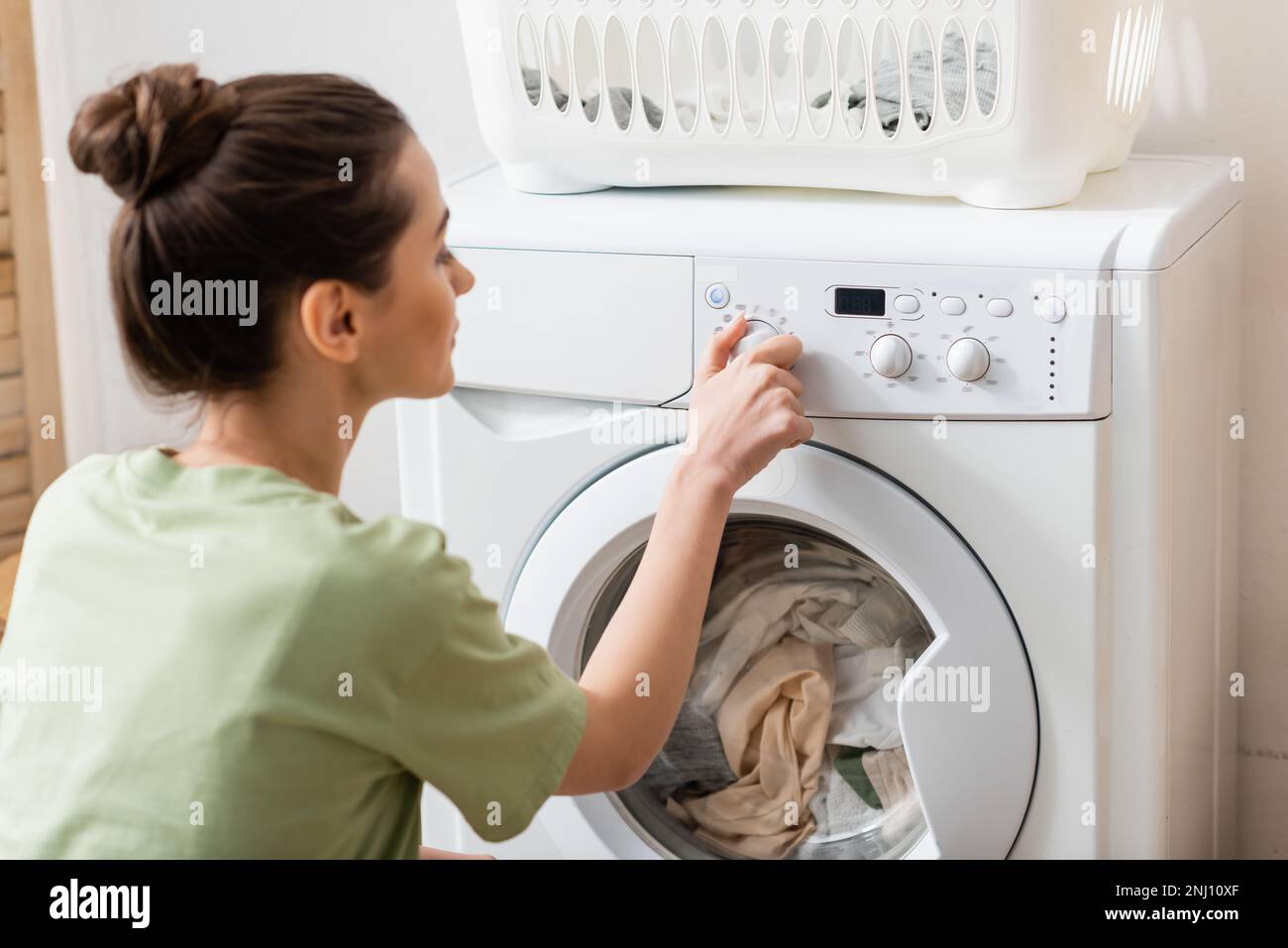 Side view of blurred woman switching washing machine near basket in ...