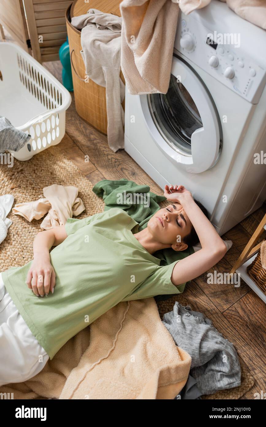 Top view of tired woman lying around clothes near washing machine in ...