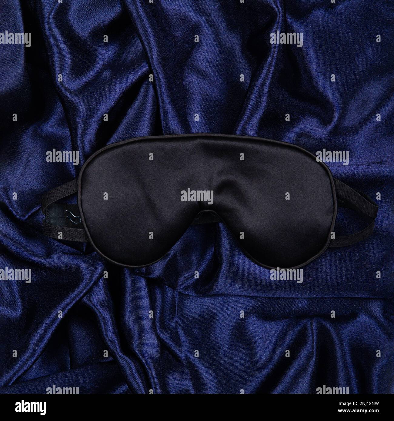 Black silk sleep mask lie on dark blue silken background. Top view ...
