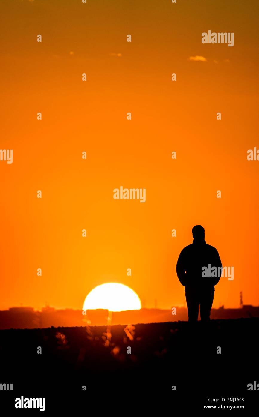 A man silhouette standing against a backdrop of a stunning sunset, his ...
