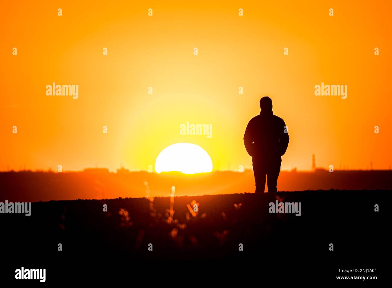A man silhouette standing against a backdrop of a stunning sunset, his ...