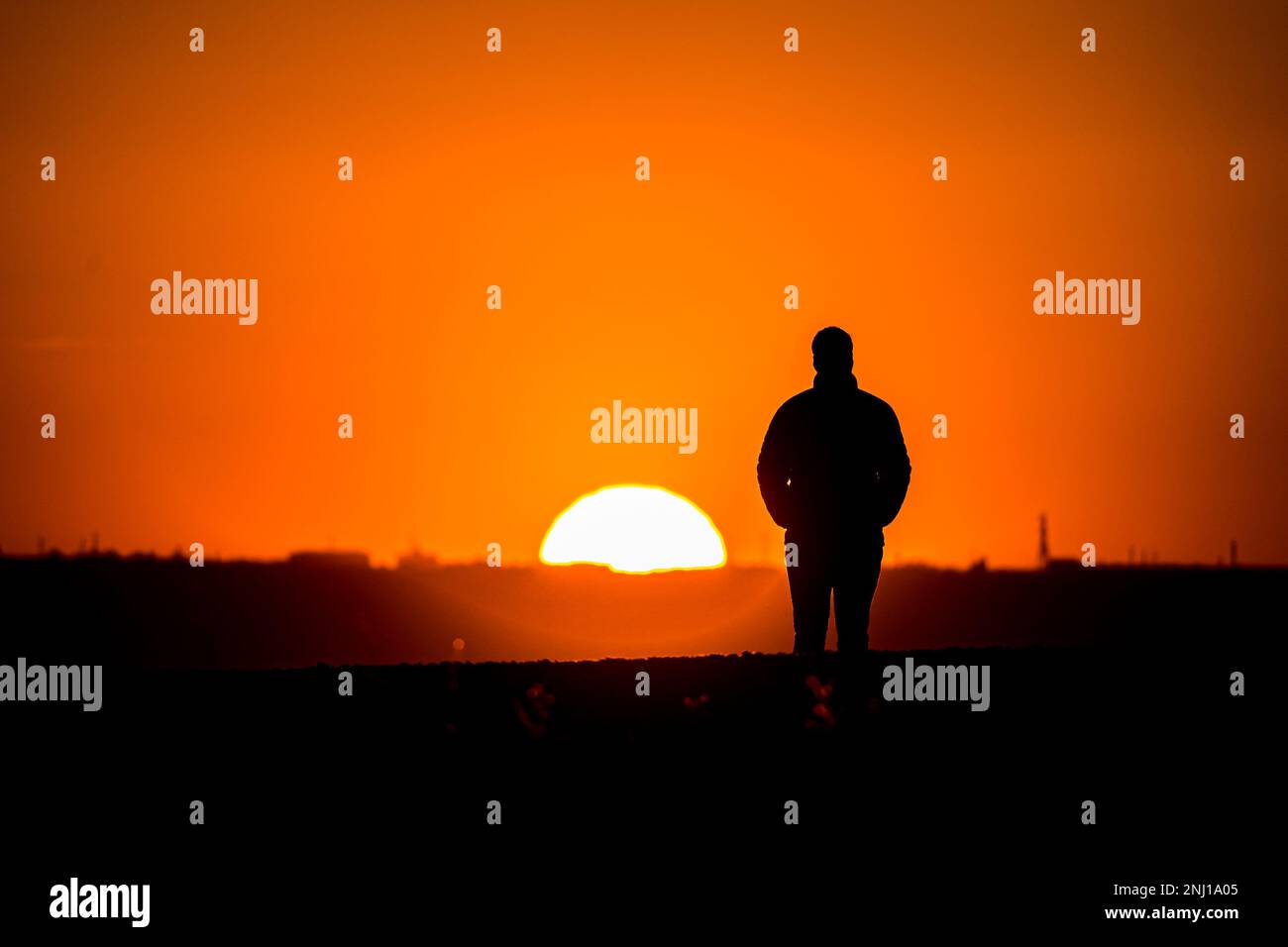 A man silhouette standing against a backdrop of a stunning sunset, his ...