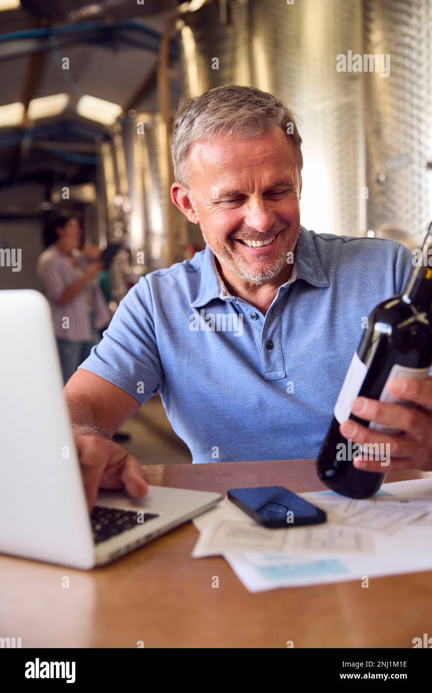Mature Man With Laptop Checking Label On Bottle Inside Winery With ...