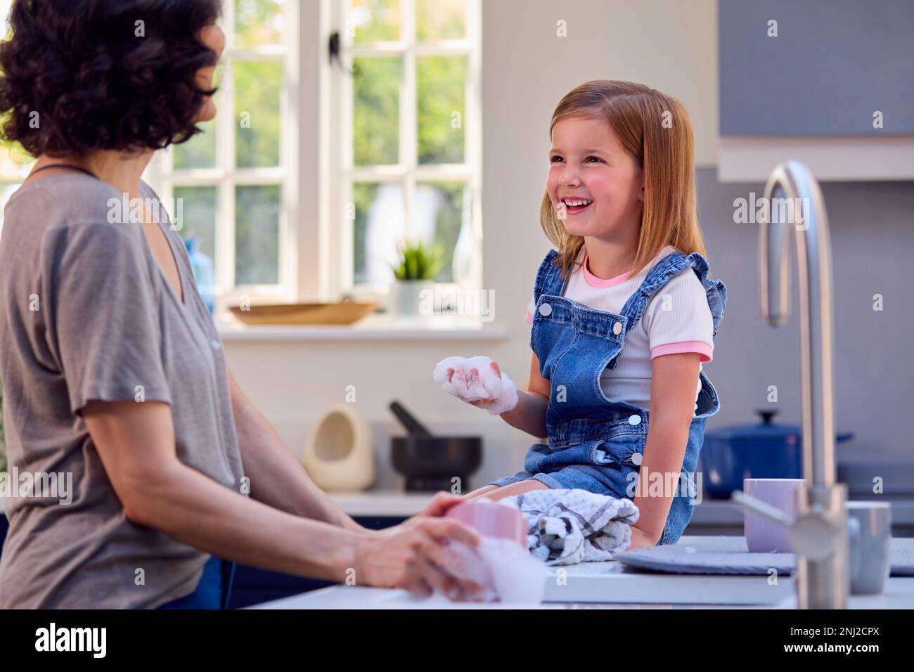 Family With Daughter Helping Older Mother To Do Washing Up In Kitchen ...