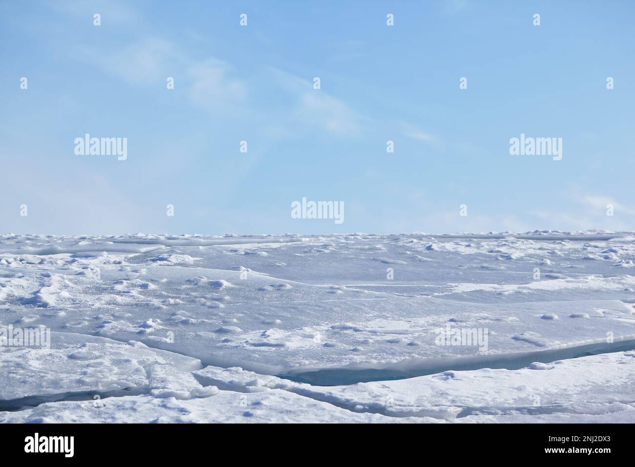 Winter ice landscape under blue sky and clouds. Cracks in the ice field ...