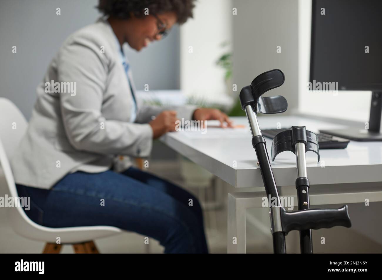 Crutches by office desk with happy disabled female employee working on ...
