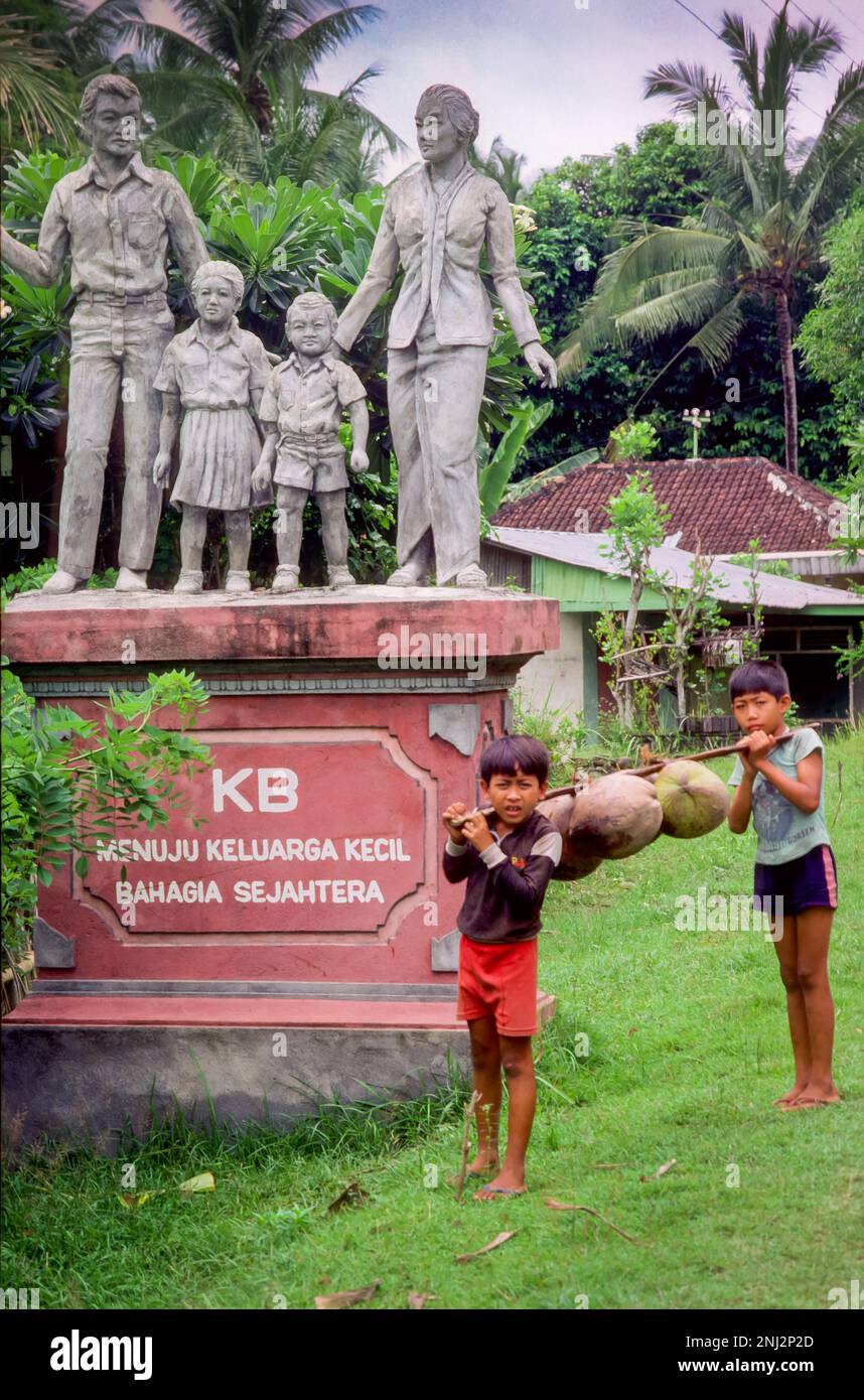 Indonesia, Java. Two boys carry fruit in front of a statue that ...