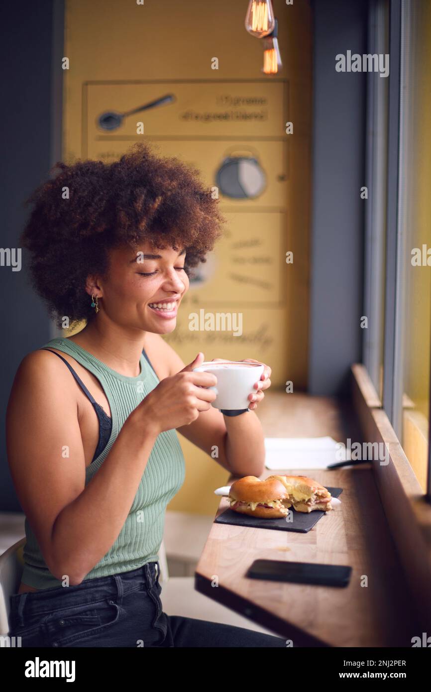 Female Customer In Coffee Shop Window Eating Bagel Sandwich For Lunch ...