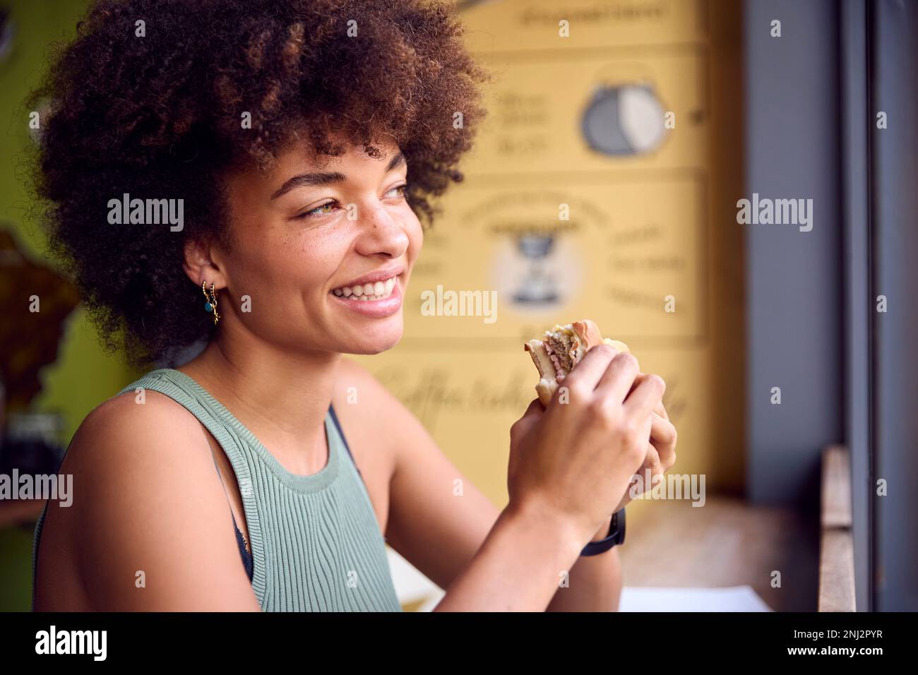 Female Customer In Coffee Shop Window Eating Bagel Sandwich For Lunch ...