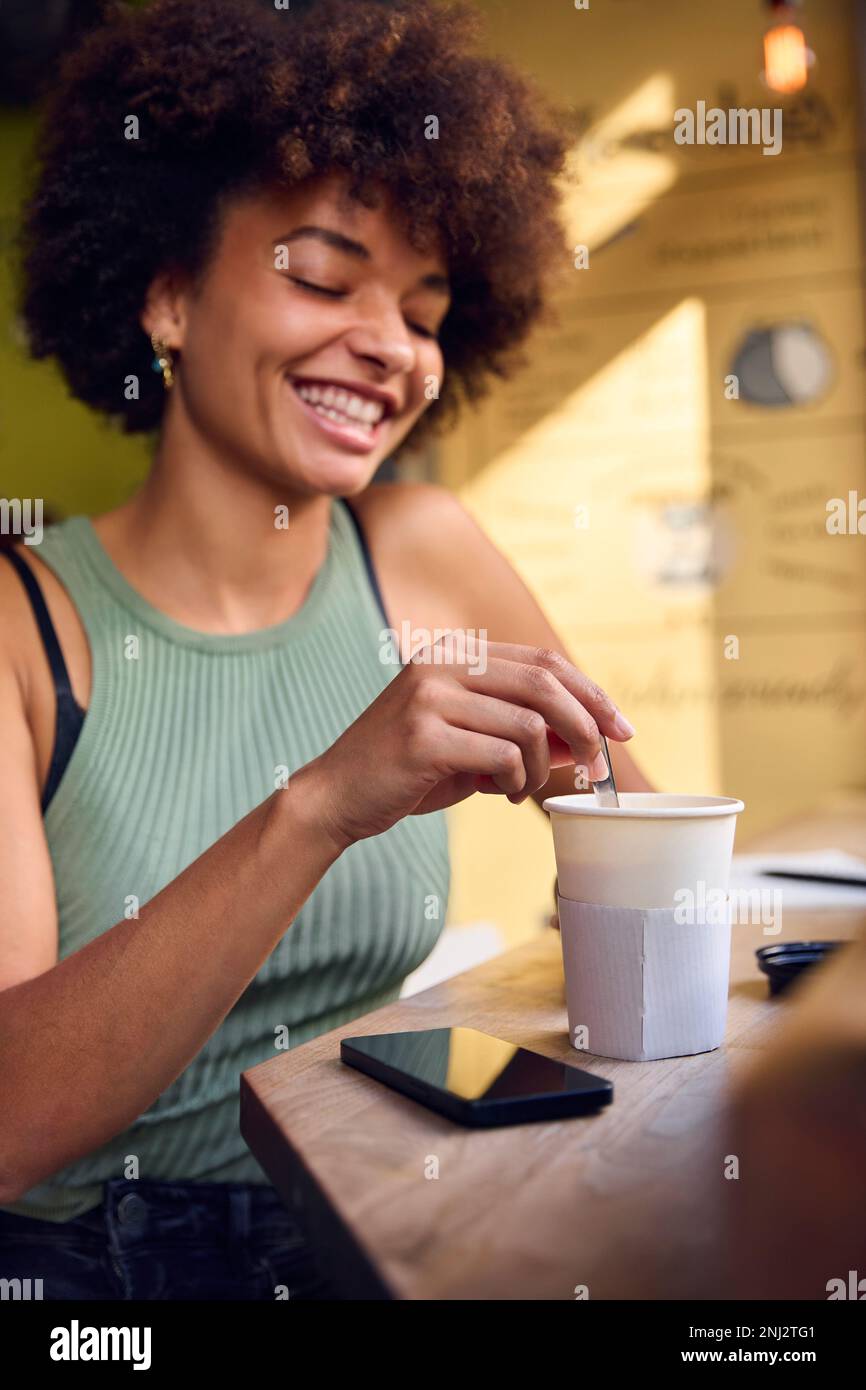 Female Customer In Window Of Cafe Stirring Hot Drink In Takeaway Cup ...