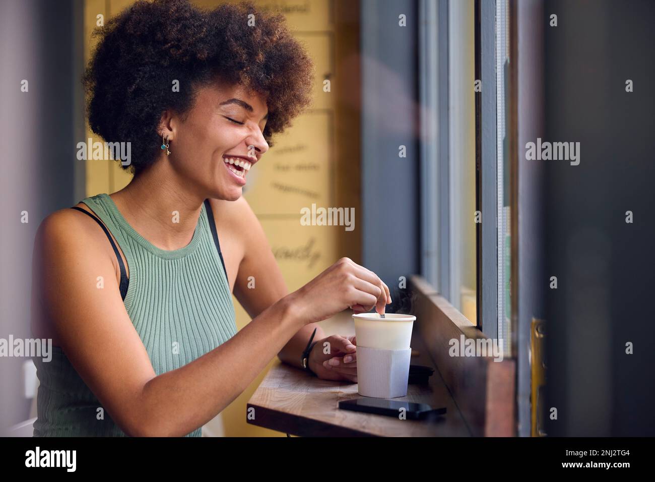 Female Customer In Window Of Cafe Stirring Hot Drink In Takeaway Cup ...