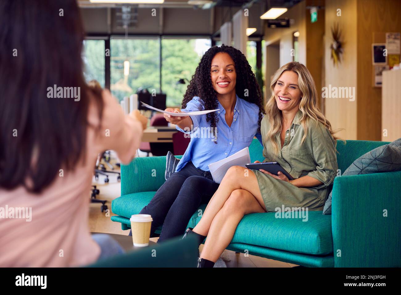 Businesswomen Having Informal Meeting In Breakout Seating Area Of ...